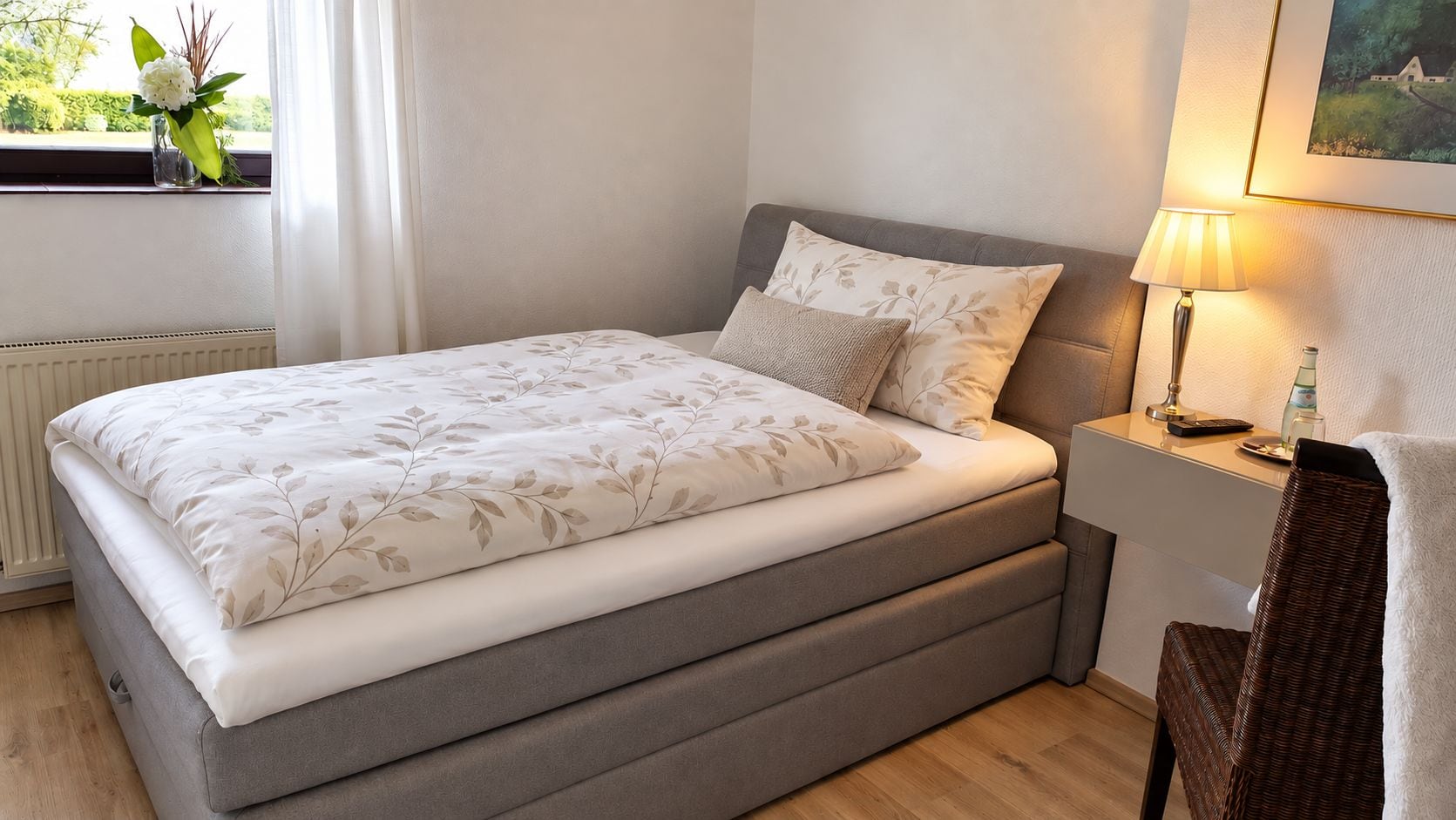 Quarto com cama, mesa de cabeceira, abajur e janela com cortinas.