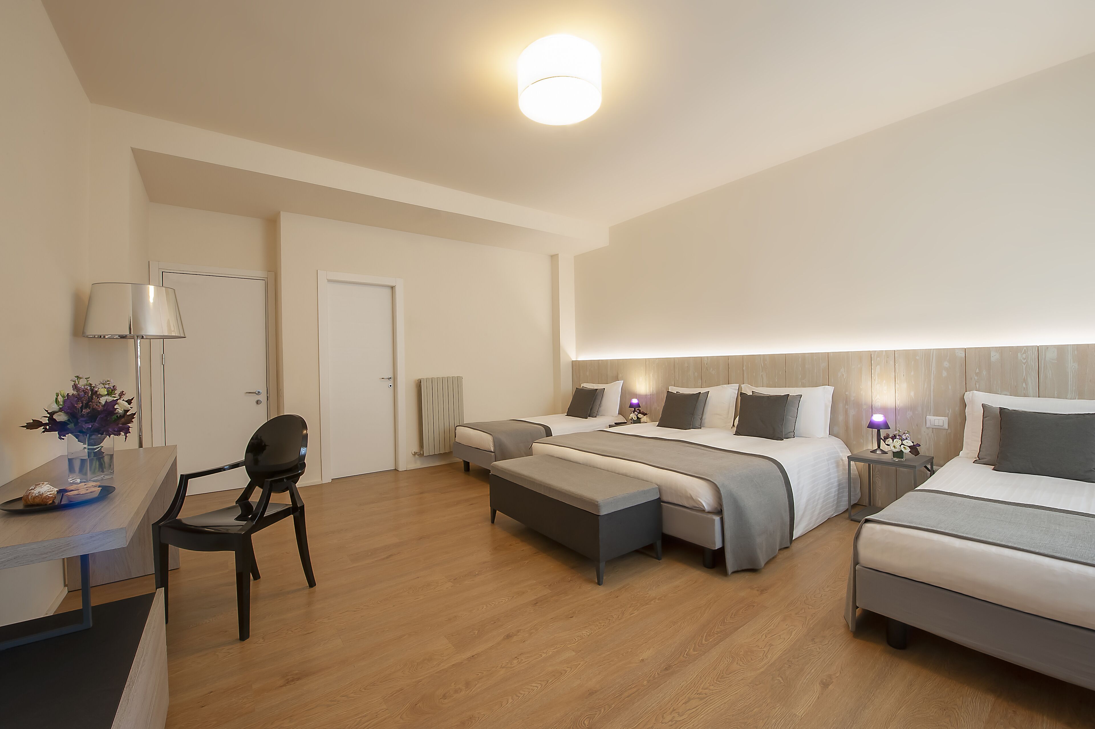 Quarto de hotel com duas camas, uma escrivaninha com cadeira e uma mesa de cabeceira com abajur.