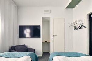 Quarto de hotel com duas camas, uma televisão, guarda-roupa e uma pequena escrivaninha.