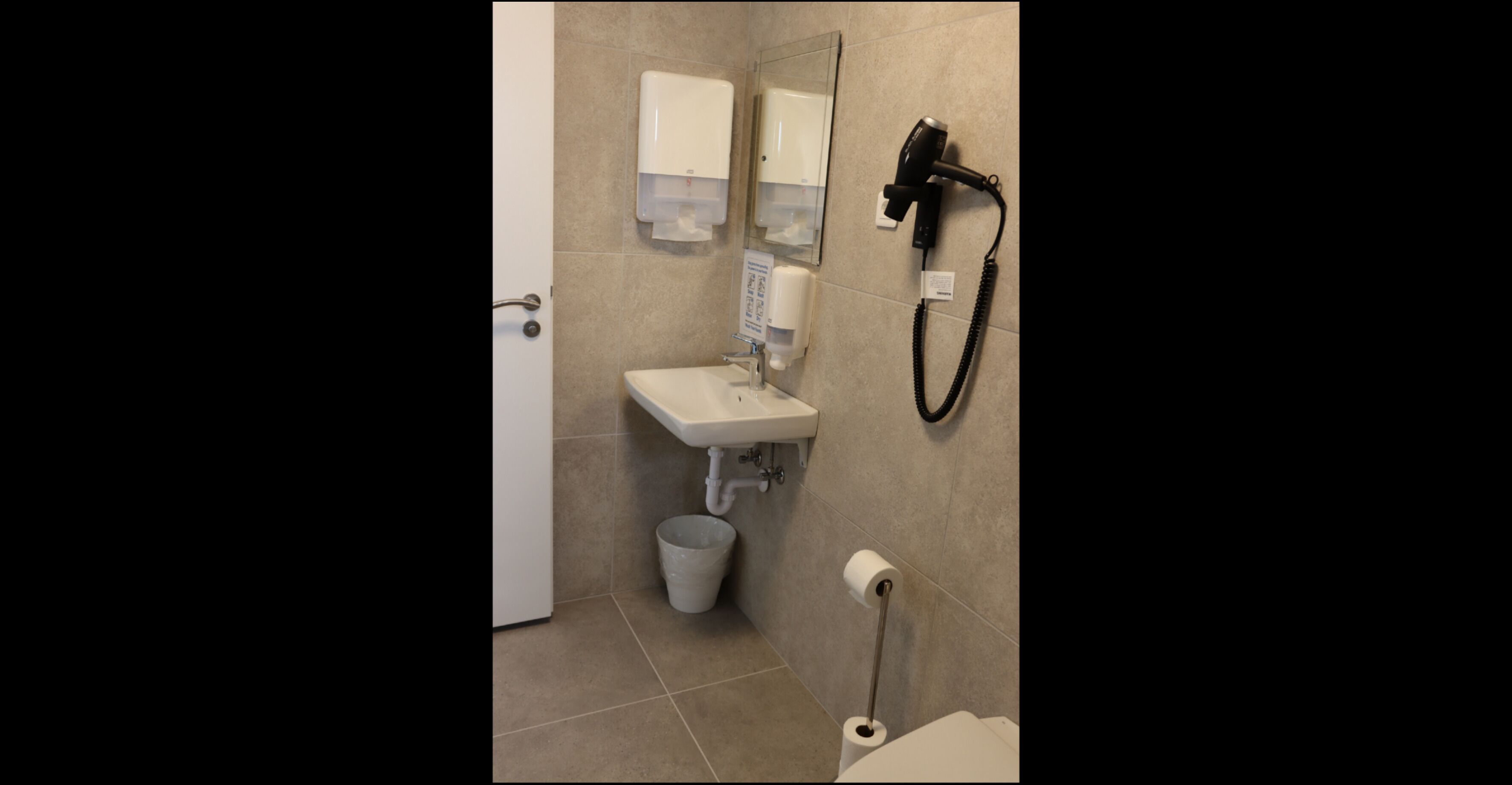 Casa de banho com lavatório, espelho, secador de cabelo e rolo de papel higiénico.