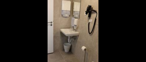 Casa de banho com lavatório, espelho, secador de cabelo e rolo de papel higiénico.