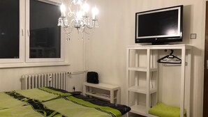 Quarto com cama, televisão em móvel, radiador, guarda-roupa branco e candelabro.