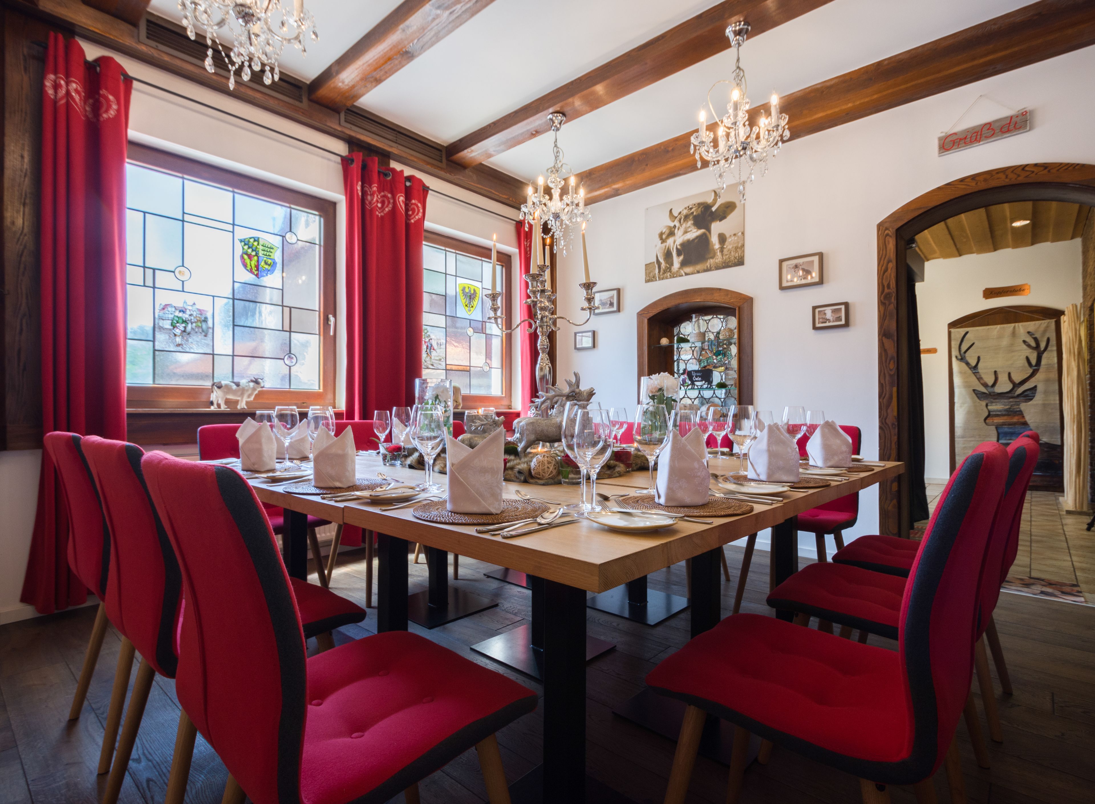 Uma sala de jantar com uma mesa comprida posta para refeição, cadeiras estofadas em vermelho e um candelabro.