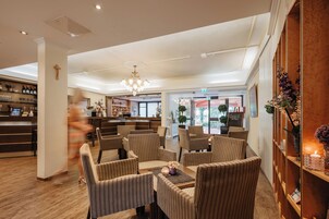 Um saguão de hotel com cadeiras listradas, um balcão de recepção, um candelabro e uma área de bar.