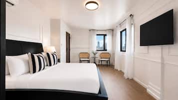 Quarto de hotel com cama grande, televisão de tela plana na parede, vista para a cidade pela janela e uma pequena mesa com cadeiras.