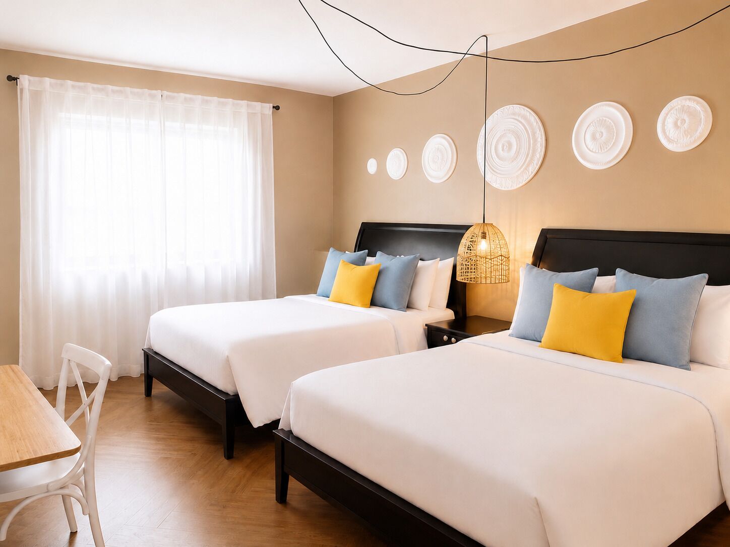 Quarto de hotel com duas camas, uma mesa de jantar e uma janela grande com cortinas translúcidas.