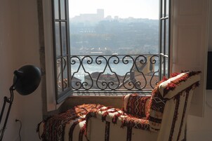 Quarto com vista para a paisagem urbana através de uma janela com grade de ferro decorativa.