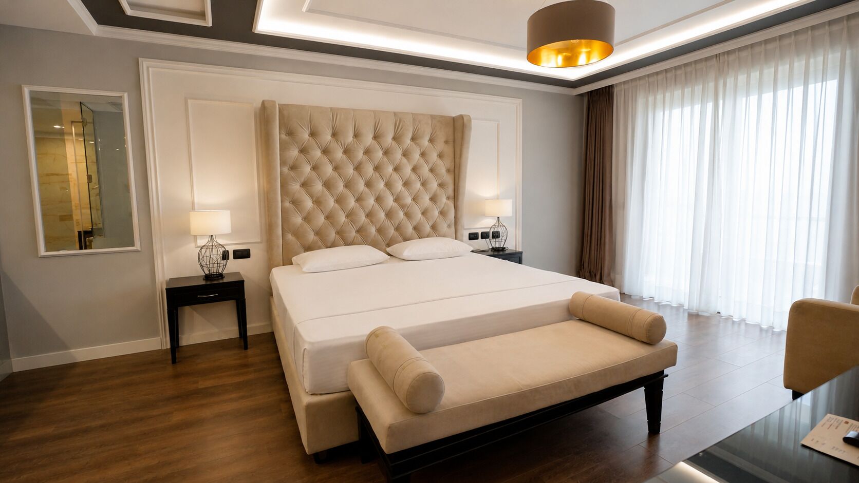 Quarto de hotel com uma cama grande, mesas de cabeceira, um banquinho e vista para o exterior.