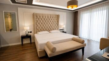 Quarto de hotel com uma cama grande, mesas de cabeceira, um banquinho e vista para o exterior.