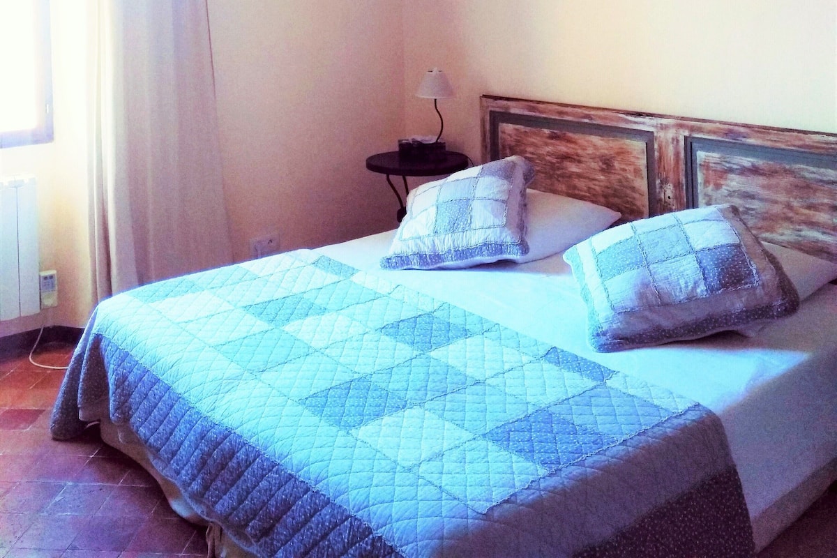 Quarto com uma cama, uma mesa de cabeceira e uma janela com cortinas.