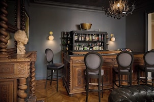 Uma área de bar com balcão de madeira, vários bancos altos e uma variedade de garrafas.