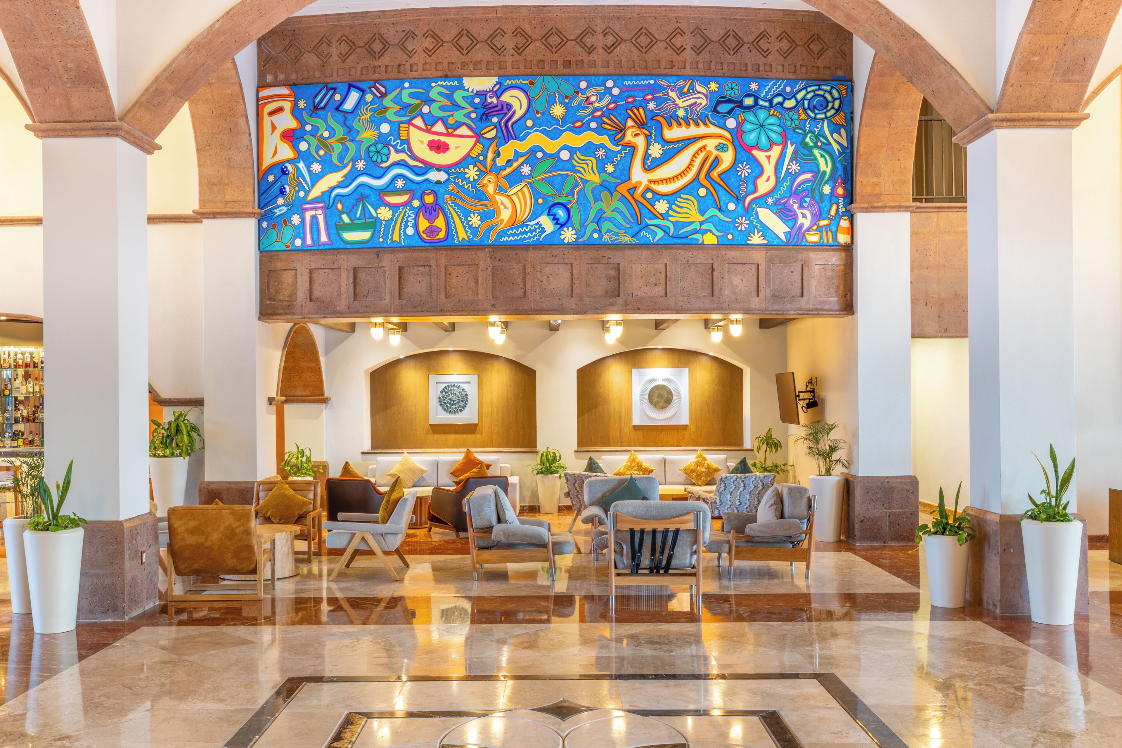 Um hall com um grande mural colorido, áreas de estar e plantas em vasos.