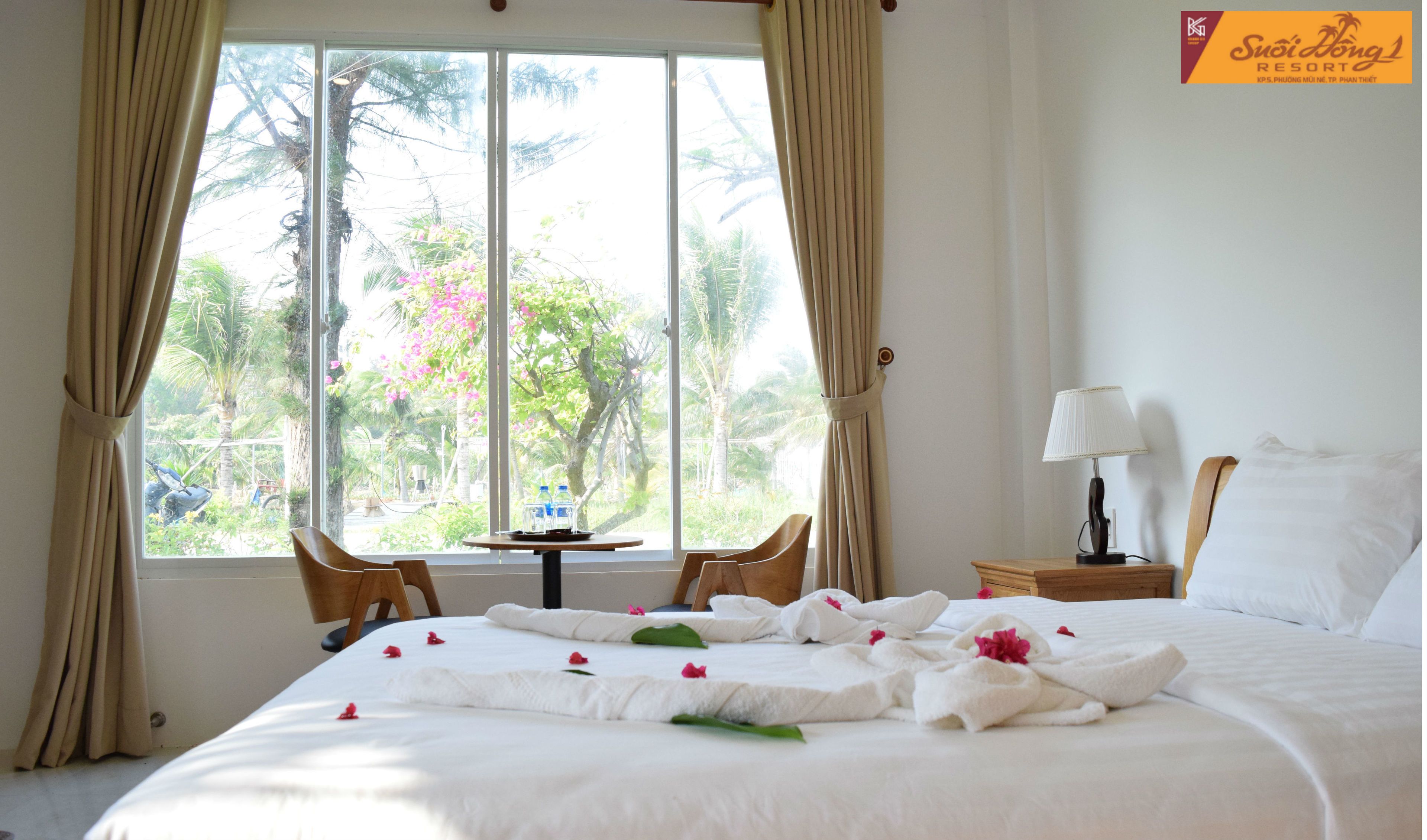 Quarto de hotel com cama, uma pequena mesa com cadeira e janela com cortinas.