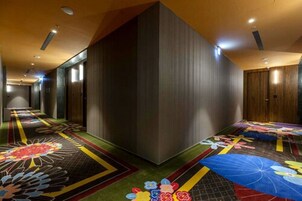 Corredor de hotel com carpete estampado, portas de madeira e iluminação embutida.