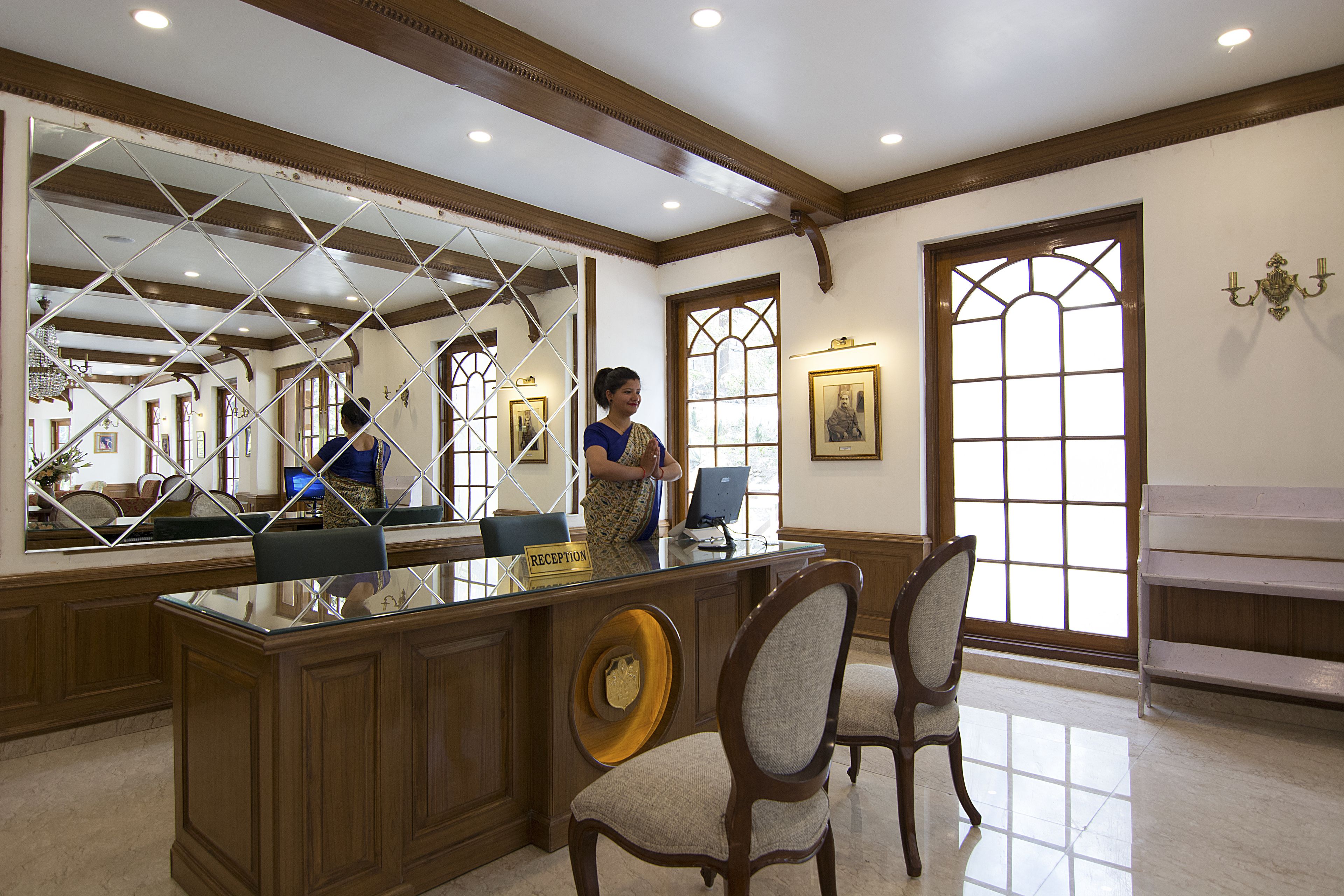 Uma área de recepção com um espelho grande, balcão de madeira, duas poltronas estofadas e um banco.