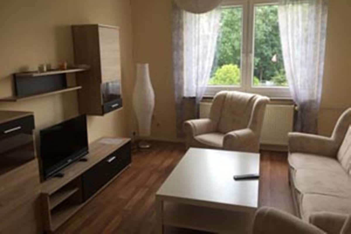 Uma sala de estar com sofá, mesa de centro, televisão e abajur.