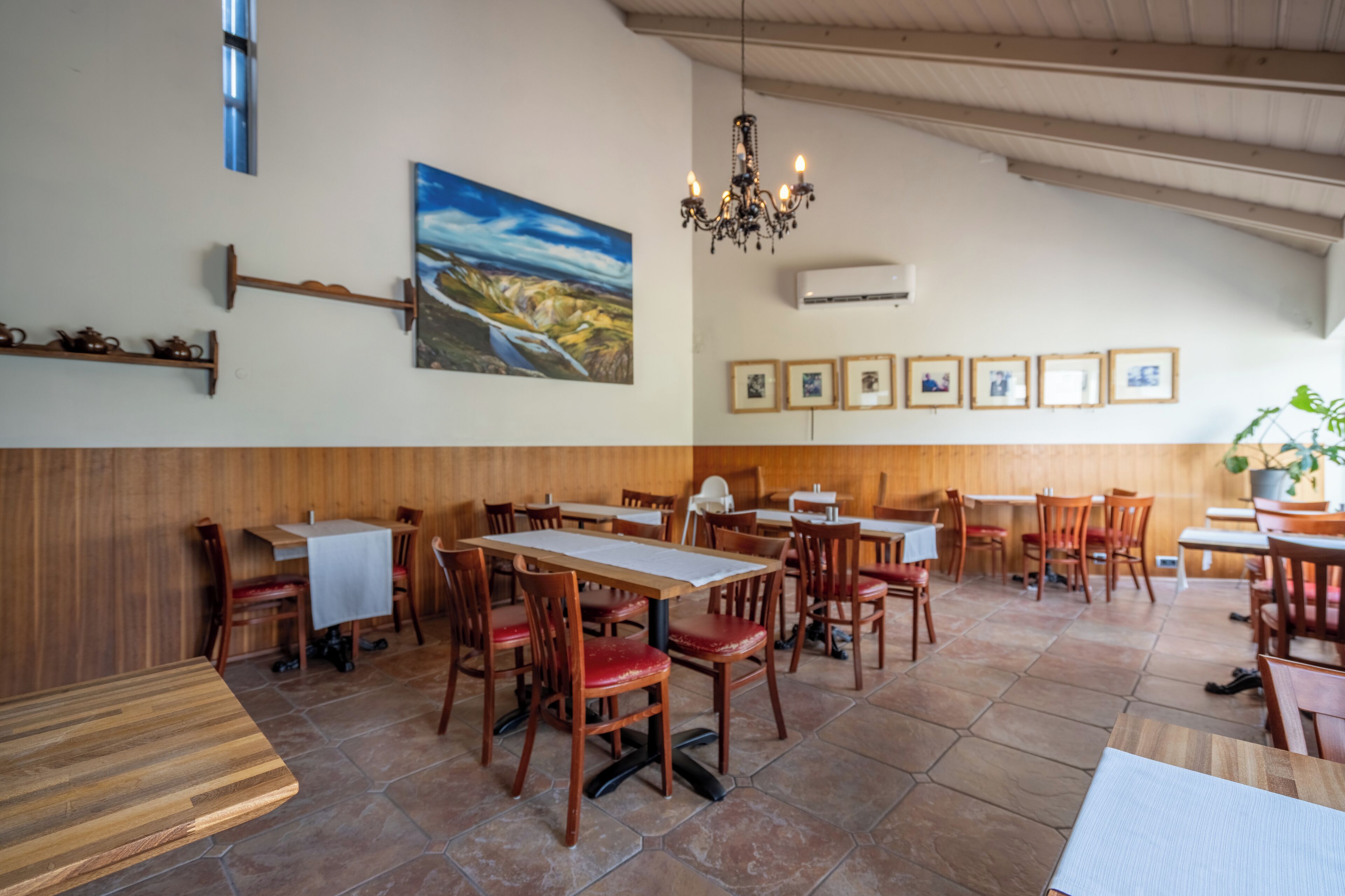 Um restaurante com mesas e cadeiras de madeira, um lustre e um quadro na parede.