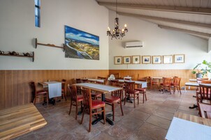 Um restaurante com mesas e cadeiras de madeira, um lustre e um quadro na parede.