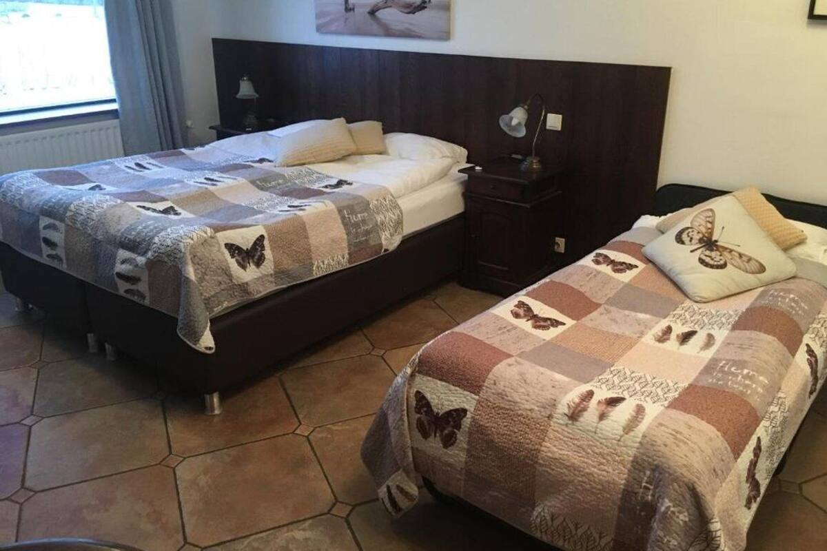 Quarto com duas camas, cada uma coberta por um edredom estampado. Tem uma mesa de cabeceira com uma luminária e um quadro pendurado na parede acima das camas.