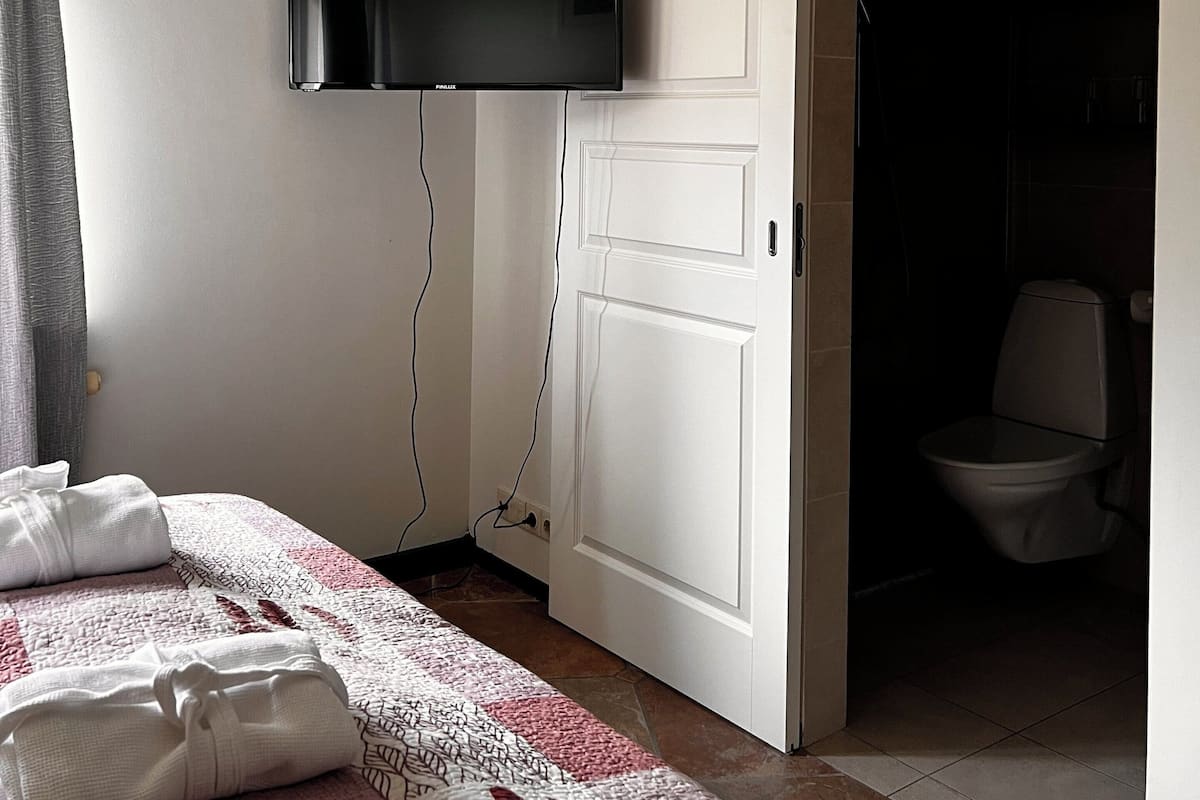 Quarto com cama, televisão de tela plana na parede, porta para um banheiro e cortina na janela.