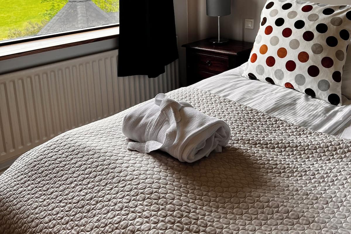 Uma cama bem arrumada com cobertura acolchoada, um travesseiro estampado com bolinhas e uma toalha dobrada sobre a cama.