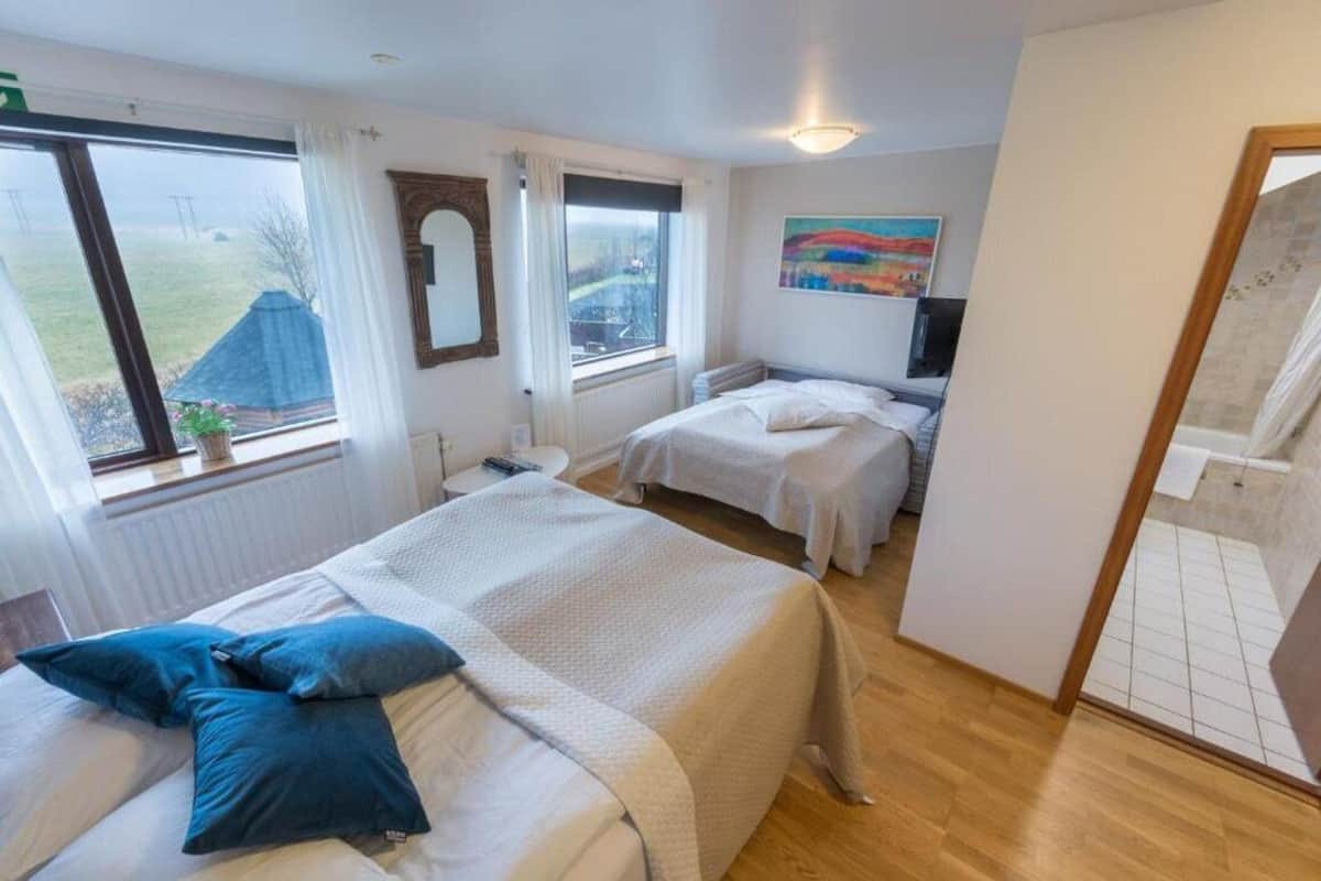 Quarto de hotel com duas camas, uma janela grande com vista para o exterior, um quadro na parede e piso de madeira.