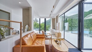 Uma sala de estar moderna com sofá de couro, mesa de centro de madeira e uma janela ampla com vista para uma paisagem montanhosa.