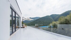 Uma varanda moderna com guarda-corpo de vidro, uma cadeira e um grande guarda-sol.