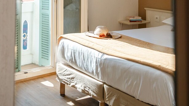 Quarto com cama, mesa de cabeceira e janela com persianas.