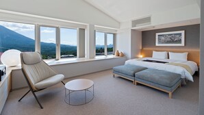Quarto de hotel moderno com uma janela grande, uma cama, um espaço para sentar e uma mesa redonda.