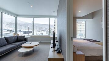Quarto de hotel moderno com uma janela grande, um sofá, uma mesa de centro redonda e uma cama.
