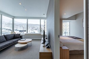 Quarto de hotel moderno com uma janela grande, um sofá, uma mesa de centro redonda e uma cama.