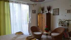 Quarto de hotel com cama, duas cadeiras de vime, uma mesinha e um armário.