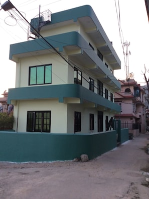 Um edifício residencial de vários andares com telhado plano, varandas e entrada com portão.