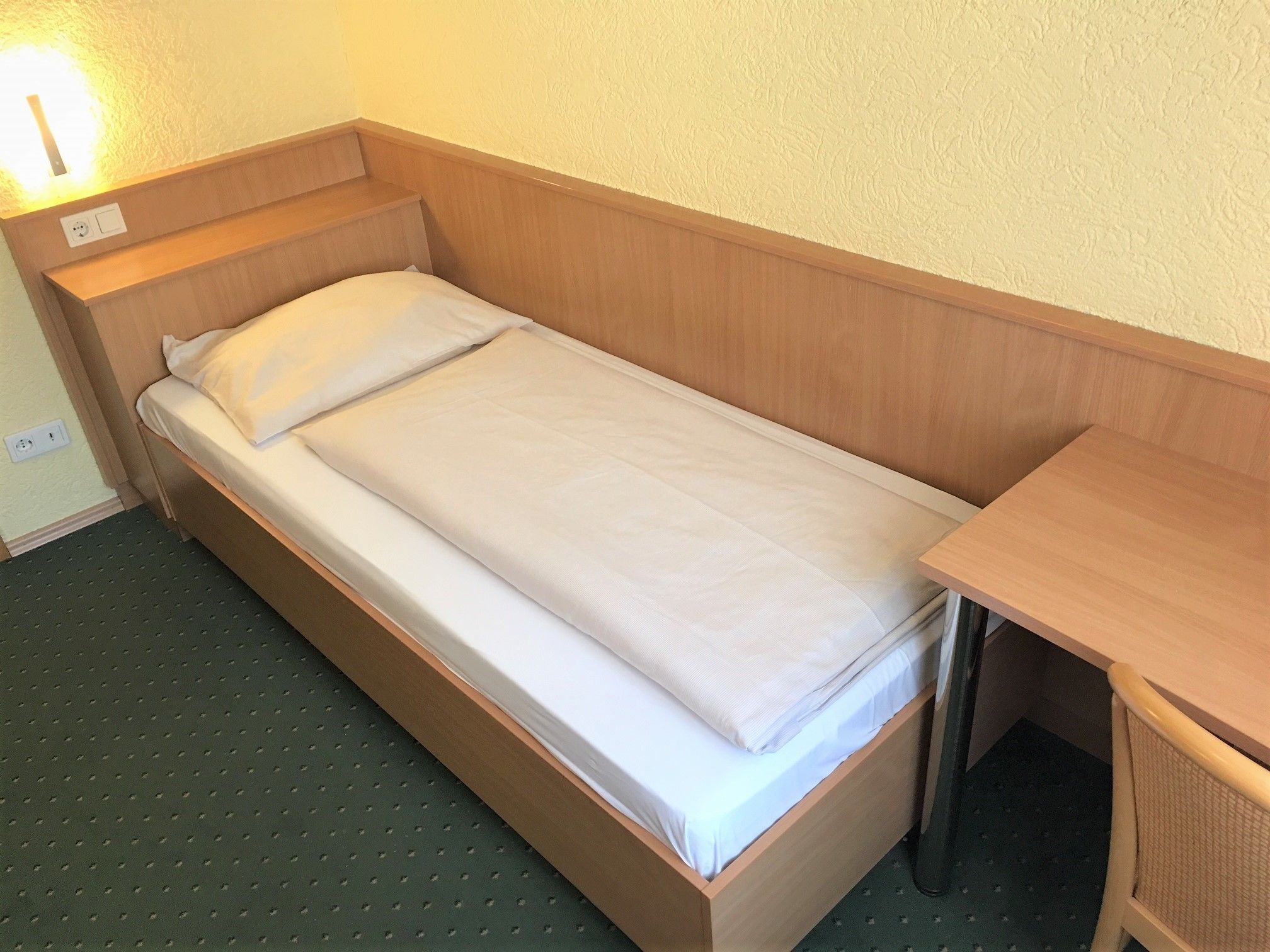 Uma cama de solteiro com cabeceira de madeira e uma mesinha de cabeceira.