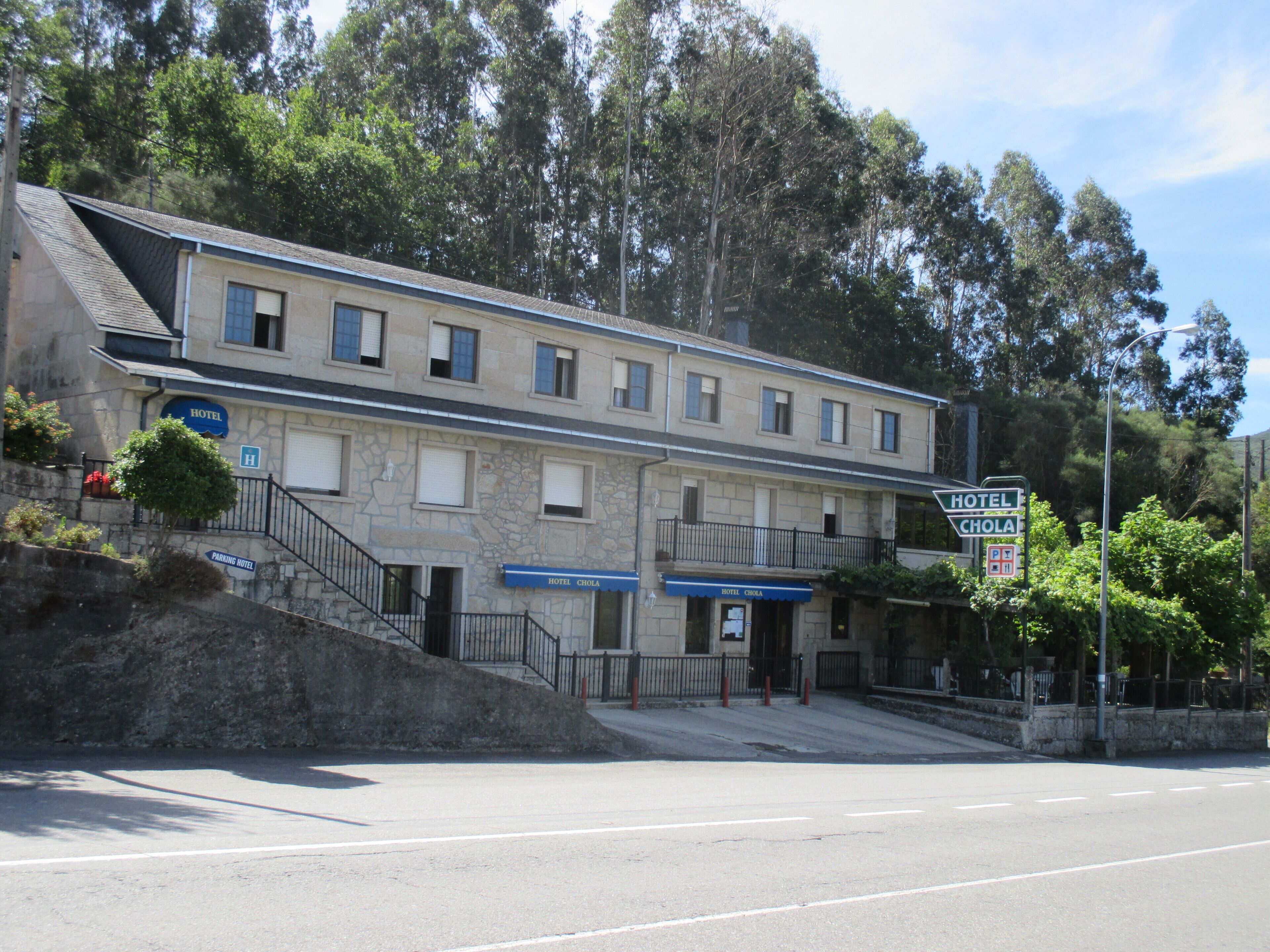 Hotel de dois andares com fachada de pedra, varanda no segundo pavimento e placa de estacionamento indicando área de estacionamento do hotel.