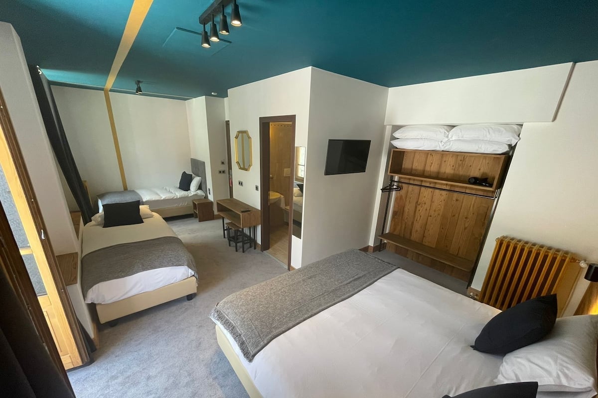 Quarto com duas camas, uma escrivaninha, um espelho, um guarda-roupa e um radiador.