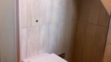 Casa de banho pequena e compacta com sanita branca, suporte de papel higiénico fixado na parede e chão em azulejos.