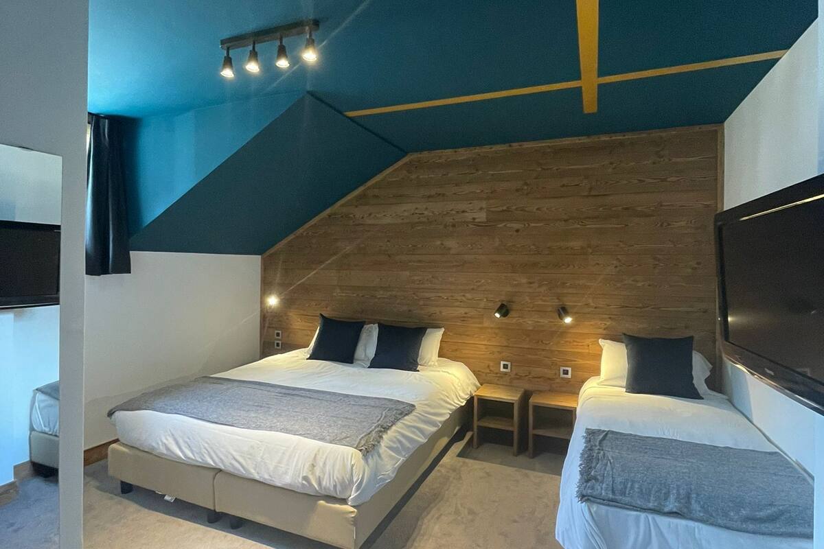 Quarto com duas camas, cabeceira de madeira e teto inclinado com iluminação embutida.