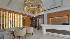 Um lobby moderno com balcão de recepção, um lustre grande, um sofá e um painel de parede estampado.