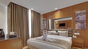 Quarto de hotel com uma cama grande, uma escrivaninha com cafeteira, televisão e espelho.