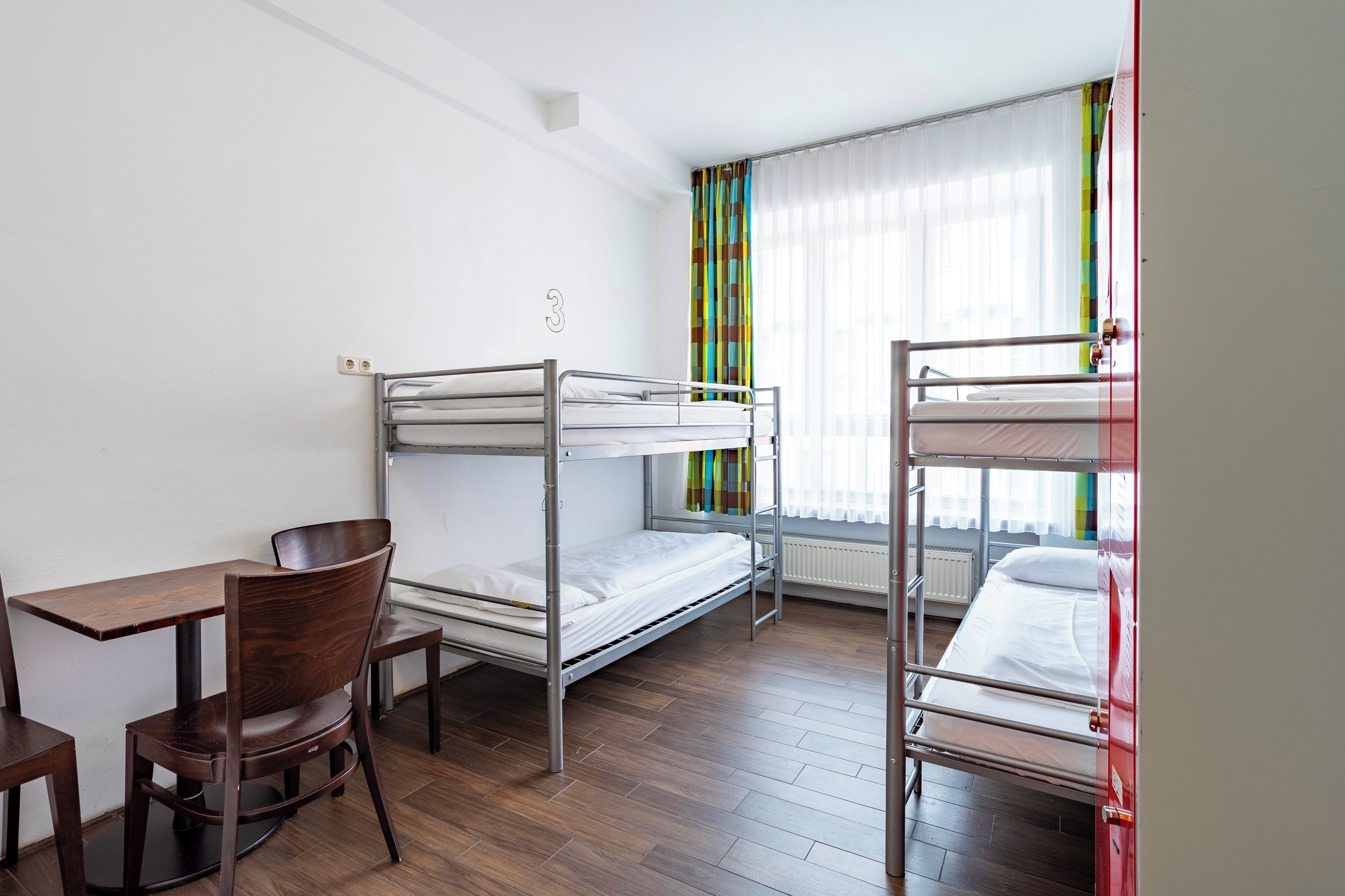 Um quarto de dormitório com beliches, uma escrivaninha de madeira e uma cadeira.