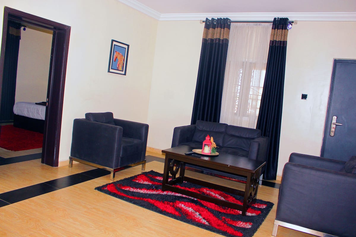 Uma sala de estar com sofá, poltronas, mesa de centro e tapete vermelho e preto.