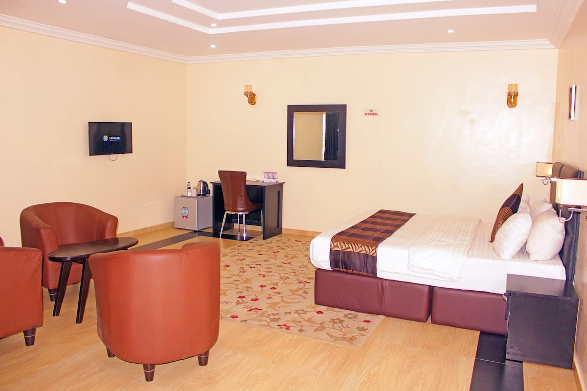 Quarto de hotel com cama, escrivaninha, cadeira e televisão.