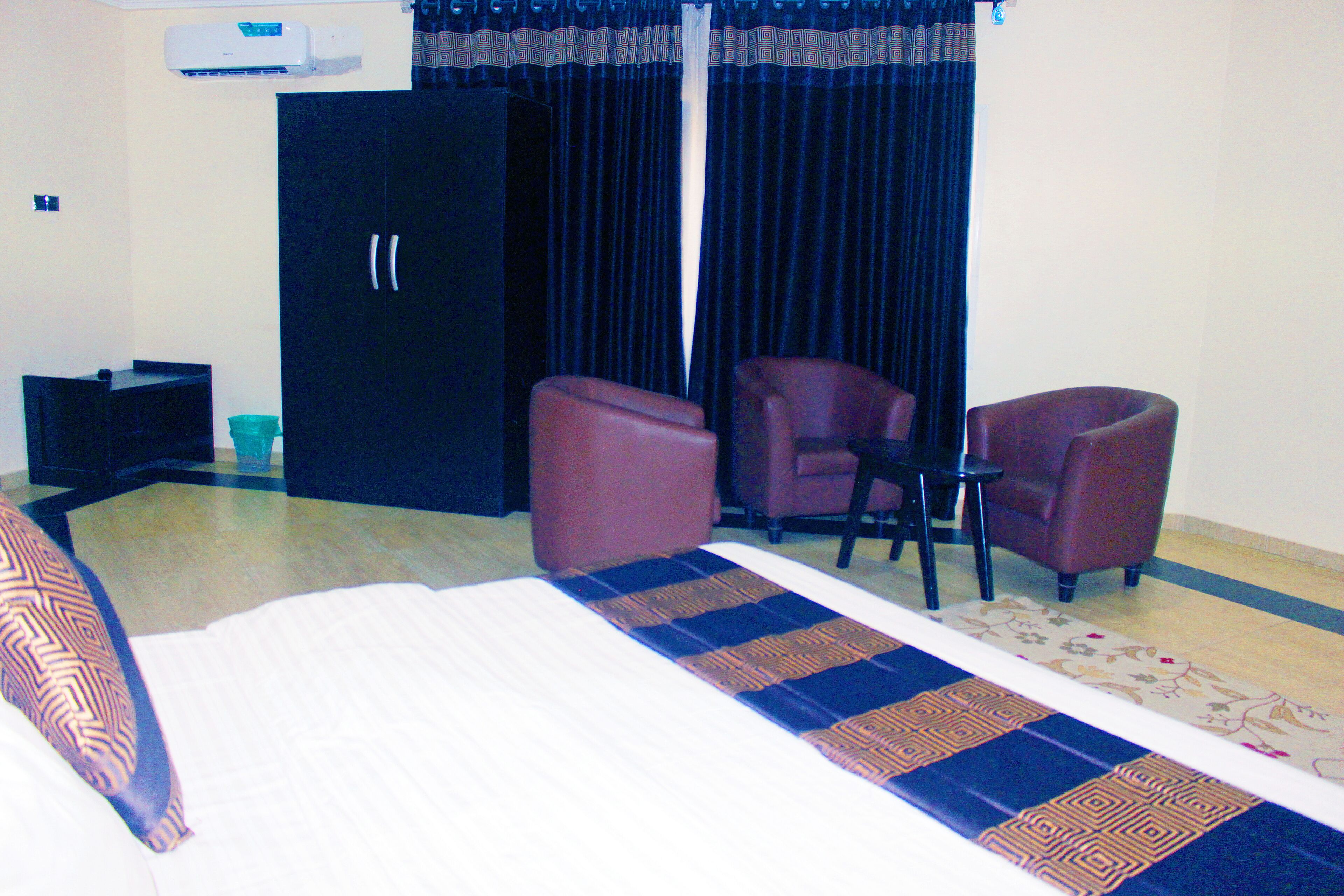 Quarto de hotel com cama, duas poltronas, uma mesinha, guarda-roupa e cortina.