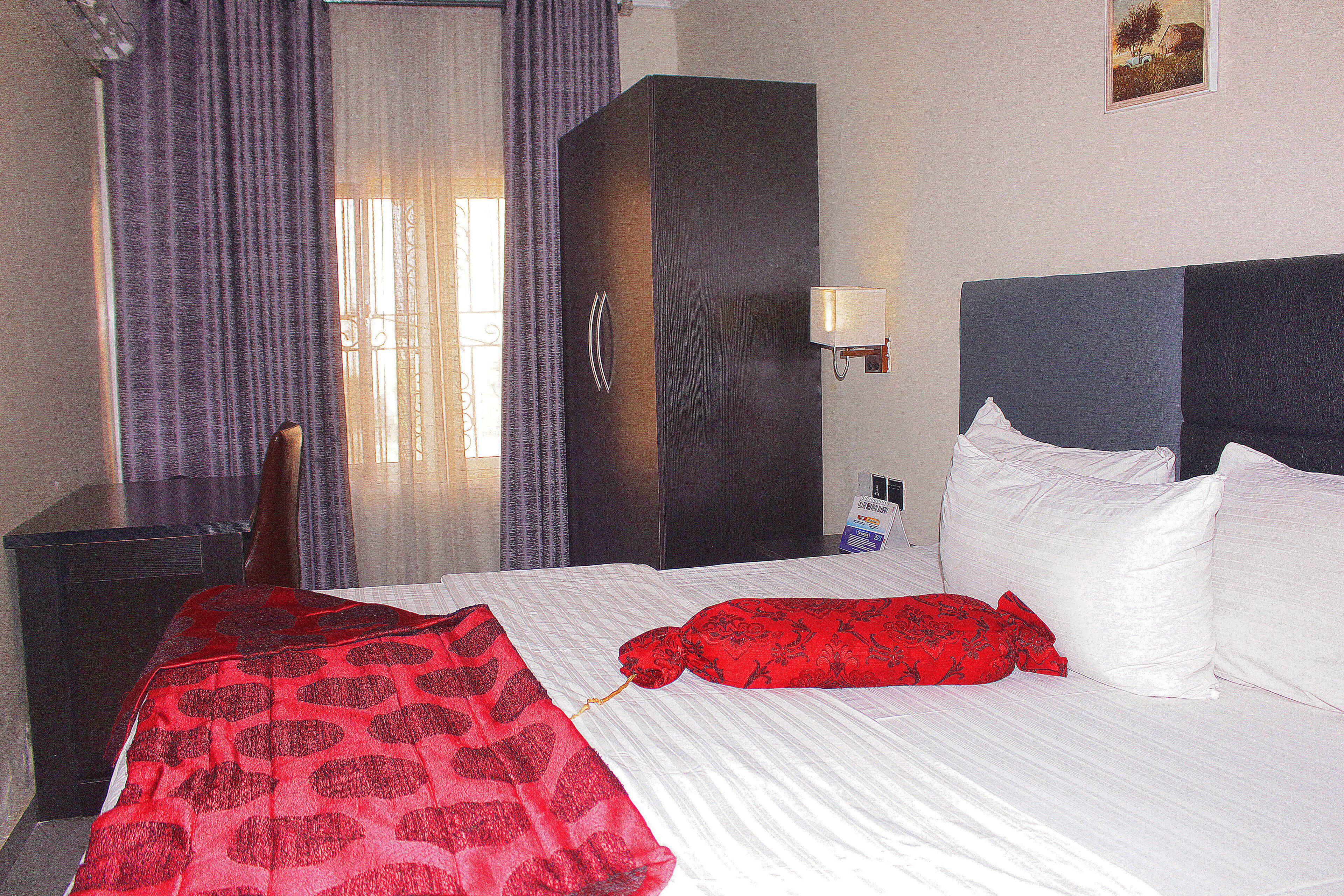 Quarto de hotel com cama, guarda-roupa, secretária e janela com cortinas.