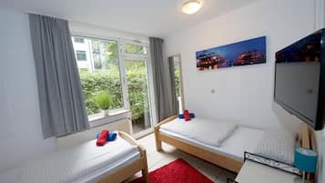 Quarto com duas camas de solteiro, televisão e janela com cortinas.