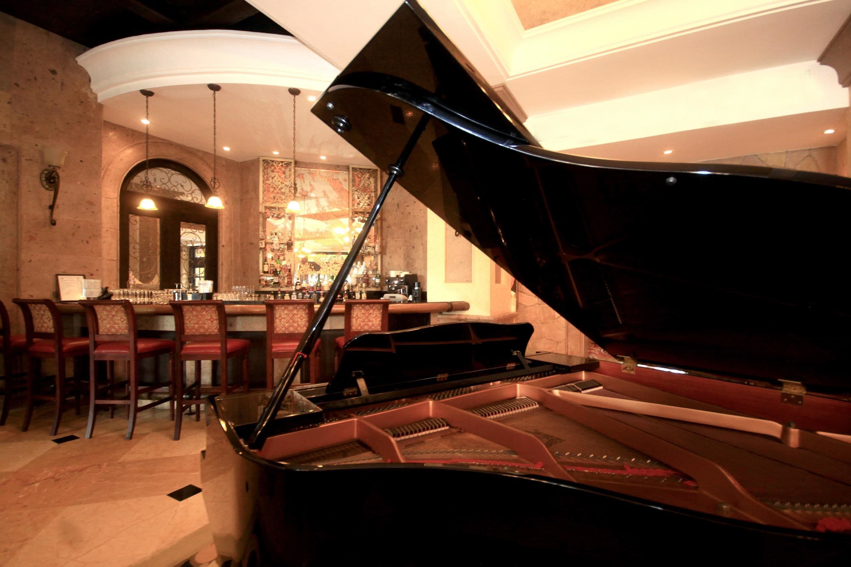 Um piano de cauda imponente numa sala bem iluminada, com espaço para bar e diversas opções de assento.