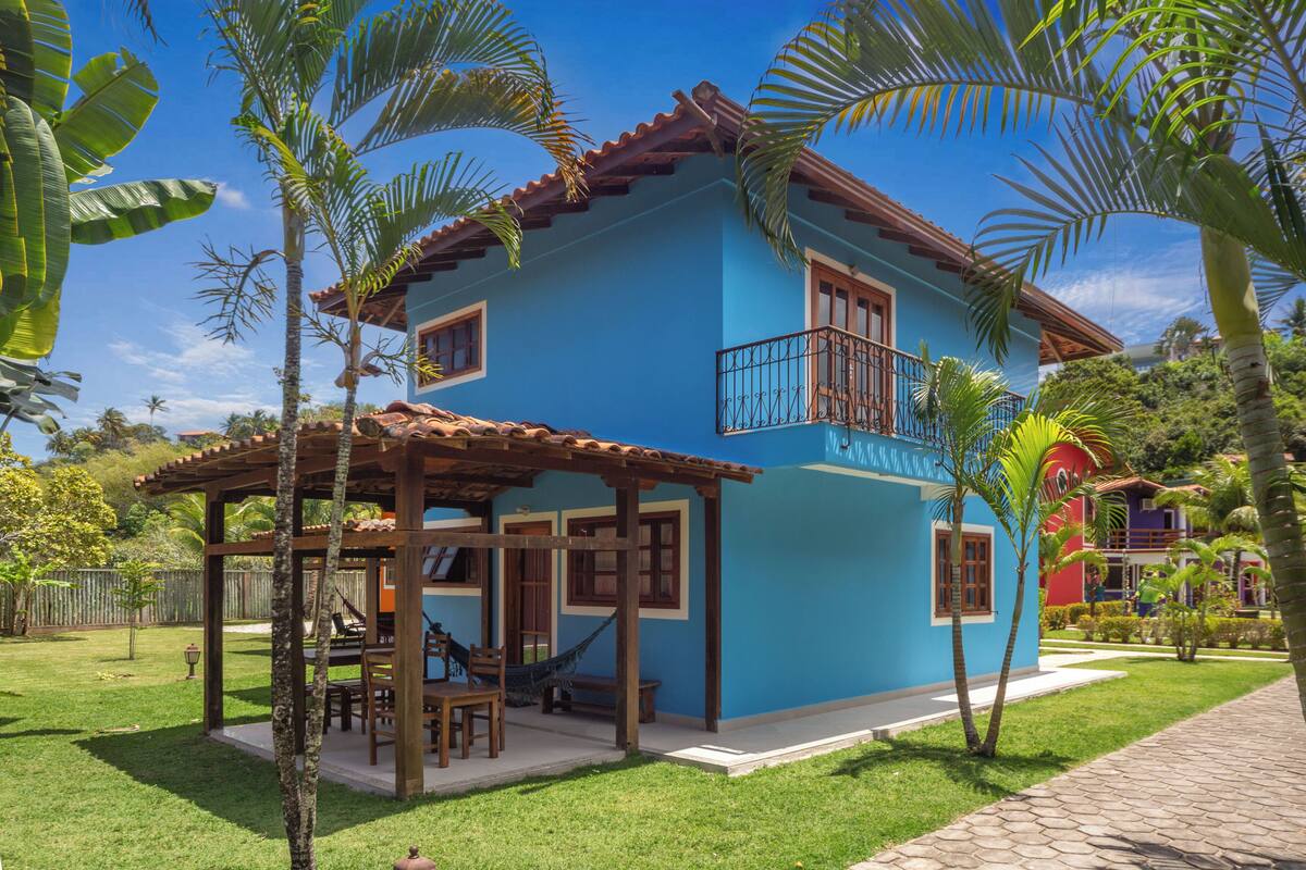 Uma casa de dois andares com varanda, pérgola de madeira e uma rede.