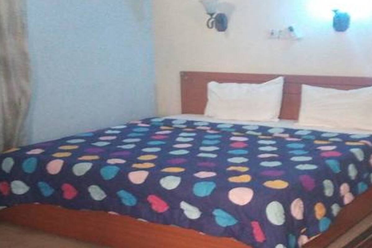 Uma cama com colcha de bolinhas, cabeceira de madeira e luminária fixada na parede.